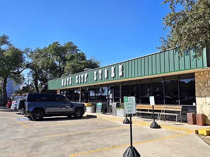 The green metal facade and shaded parking promise a laid-back Hill Country meal under ancient oak trees.