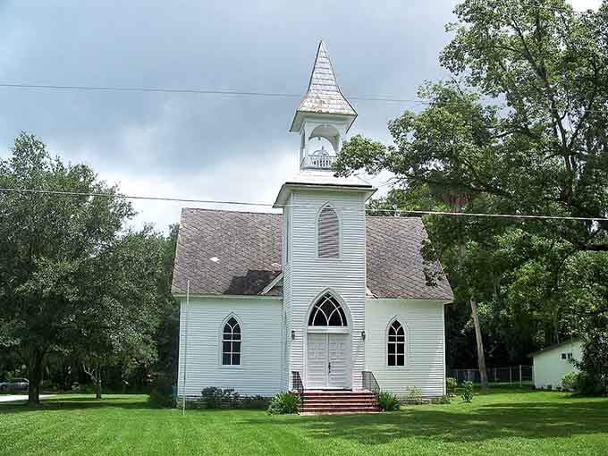 A classic white steeple church sits peacefully among the trees, looking exactly like every small-town postcard you've ever loved.