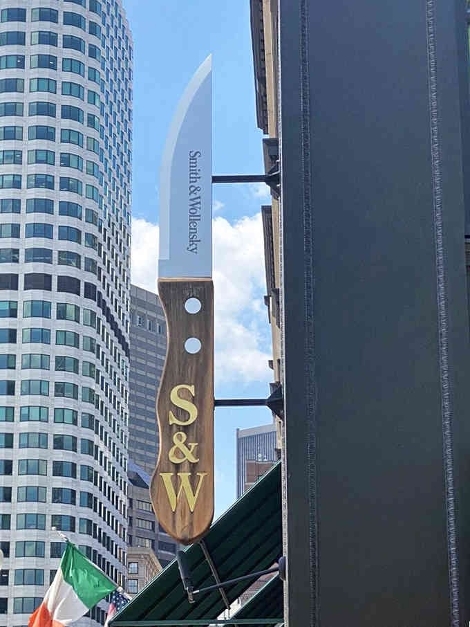 That iconic steak knife sign cuts through Boston's skyline like a delicious promise hanging above the bustling streets.
