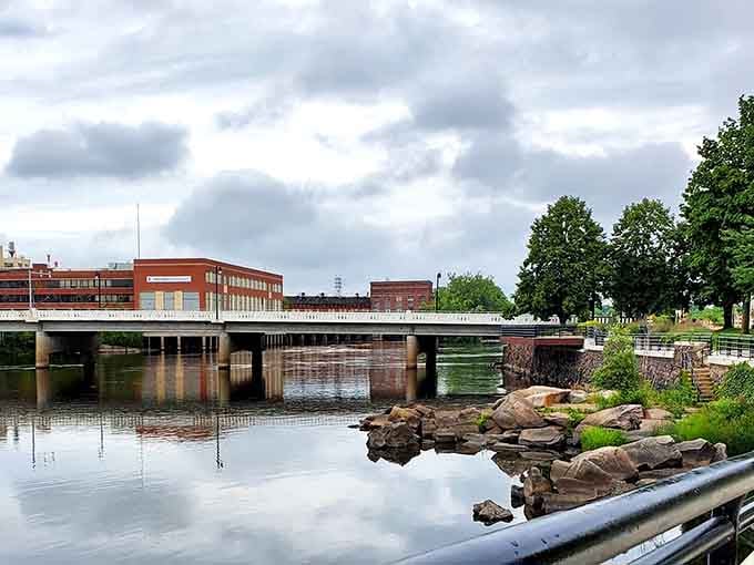 The river mirrors dramatic clouds while the bridge connects past to present in this perfectly composed small-town tableau.