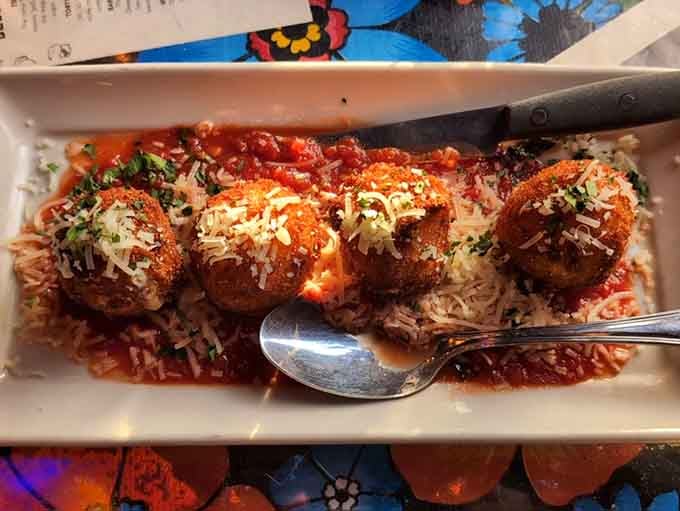 These golden arancini balls nestle in marinara like edible treasures waiting to reveal their creamy risotto centers.