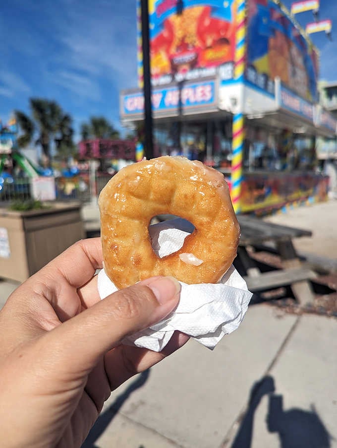 Holding happiness: that golden ring of fried dough with carnival colors blurred behind tells the whole story.