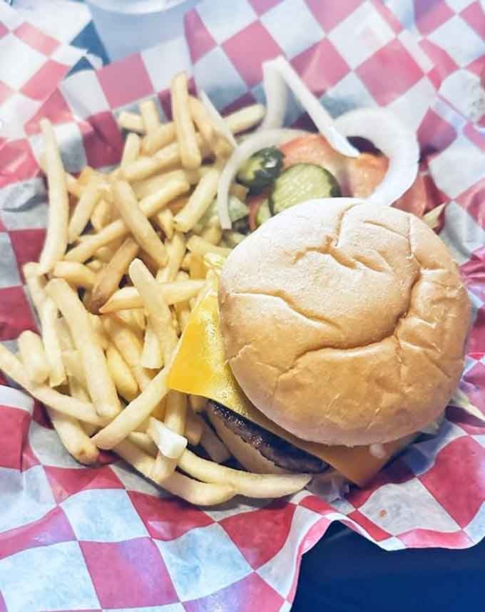 Classic cheeseburger with pickles and fries on checkered paper, the kind of meal that never goes out of style.