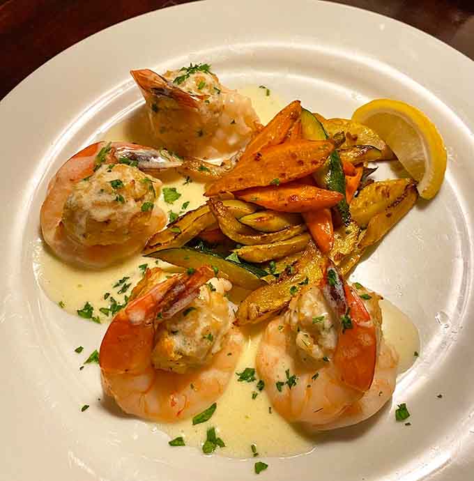 Plump baked stuffed shrimp swimming in butter sauce with colorful vegetables make every bite feel like a coastal celebration.