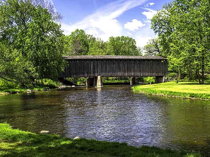 Lush green trees frame your view of a rustic timber bridge as it stretches peacefully across the calm, shimmering river.