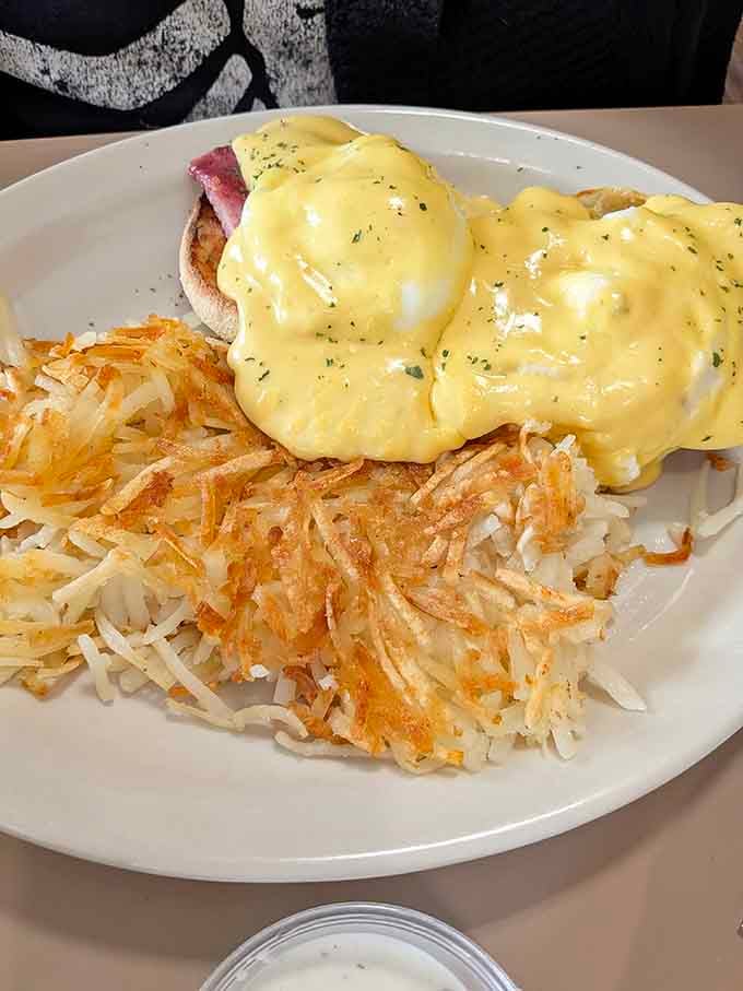 Eggs Benedict with hollandaise that cascades like a delicious yellow waterfall over perfectly poached eggs and crispy hash browns.
