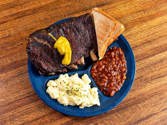 Ribs, beans, and potato salad on a blue plate&mdash;the holy trinity of barbecue happiness served family-style perfection.