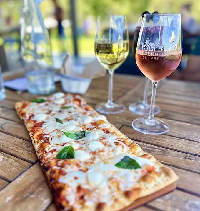 Flatbread and wine on a wooden table overlooking the vineyard&mdash;this is what "living your best life" actually looks like in practice.