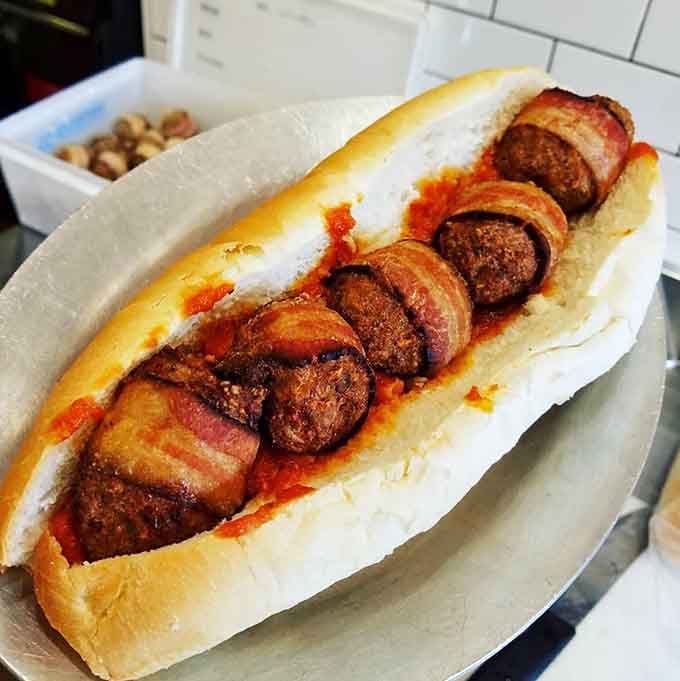 Bacon-wrapped meatballs nestled in a roll with sauce dripping down, this is what hot dog dreams are made of.
