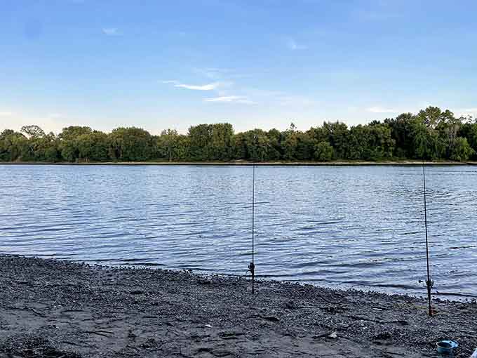 Two fishing rods stand sentinel on this quiet shore, waiting patiently while the river whispers its timeless secrets.