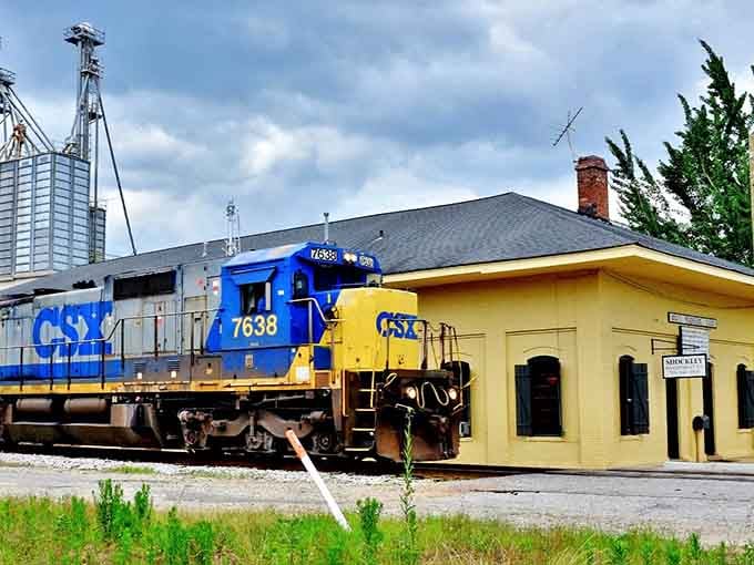 That bright blue and yellow locomotive against the cream depot creates a color combination that photographers dream about.