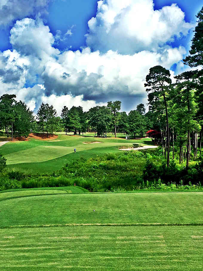 Dramatic clouds tower over emerald fairways framed by towering pines, creating a golfer's paradise or photographer's dream.