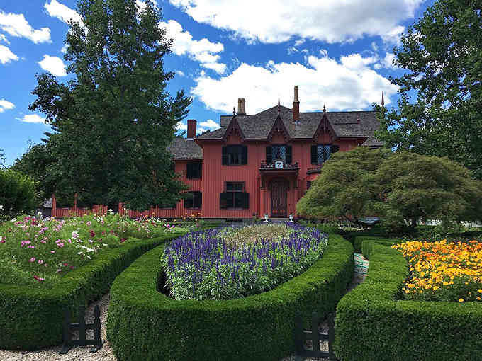 The pink Gothic cottage stands proudly amid perfectly sculpted hedges and vibrant flower beds bursting with purple and gold blooms.