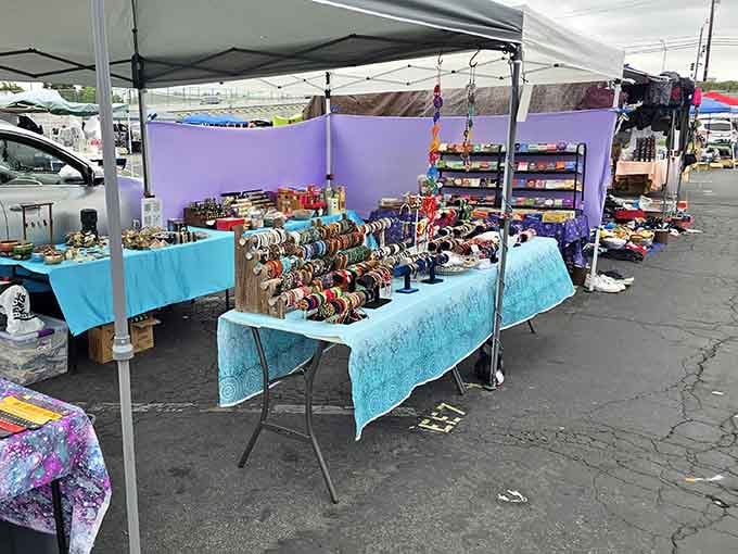 Colorful bracelets catch the light like tiny rainbows organized neatly on tables beneath protective purple canopies overhead.