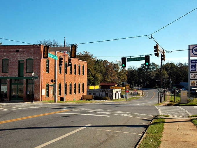Empty brick buildings watch the intersection where traffic lights change for nobody, performing their duty to an absent audience.