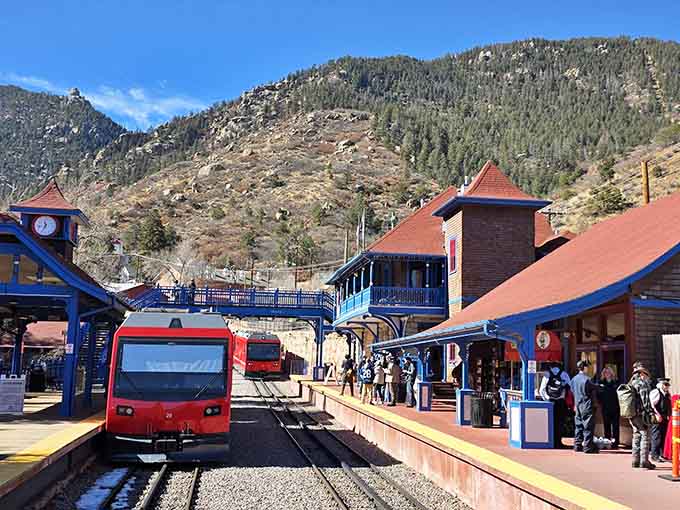 The bright red modern cog railway train waits at the charming blue-trimmed Manitou Springs station, mountains towering protectively behind.