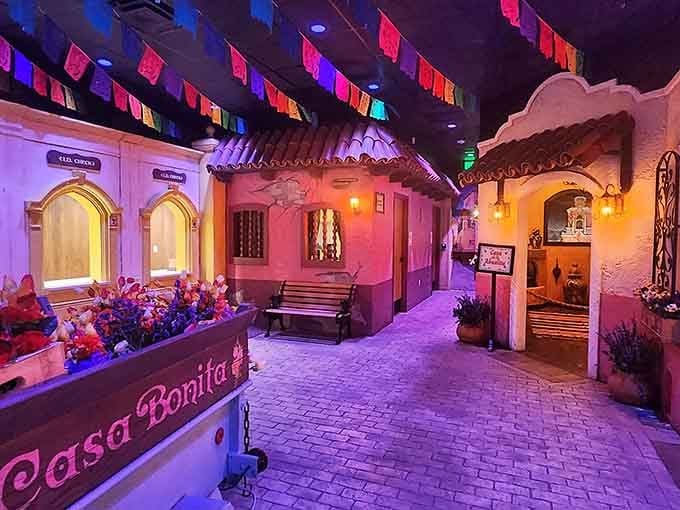 The indoor village streets glow with warm light, creating a Mexican fantasy world where cliff divers perform during dinner service.