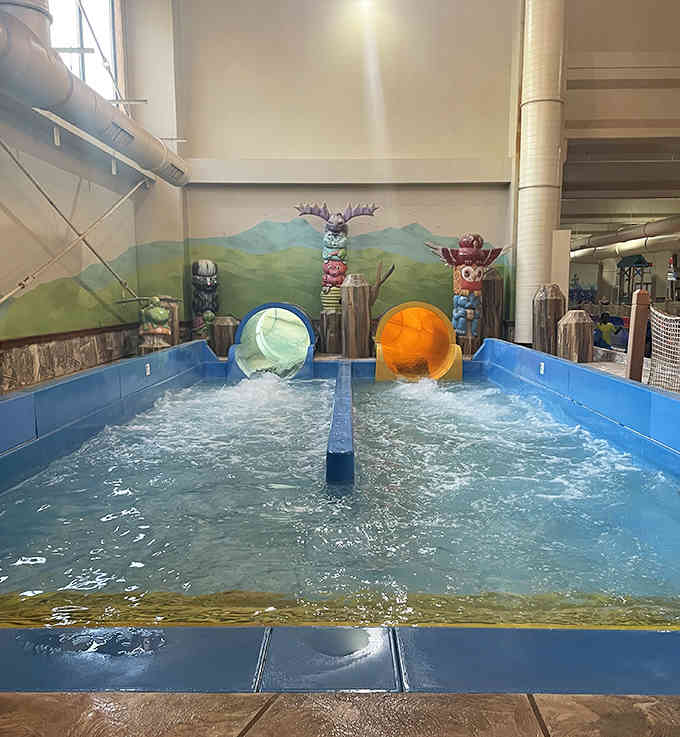 Two colorful spheres race down side-by-side slides, ready to splash into mountain-themed indoor excitement below.