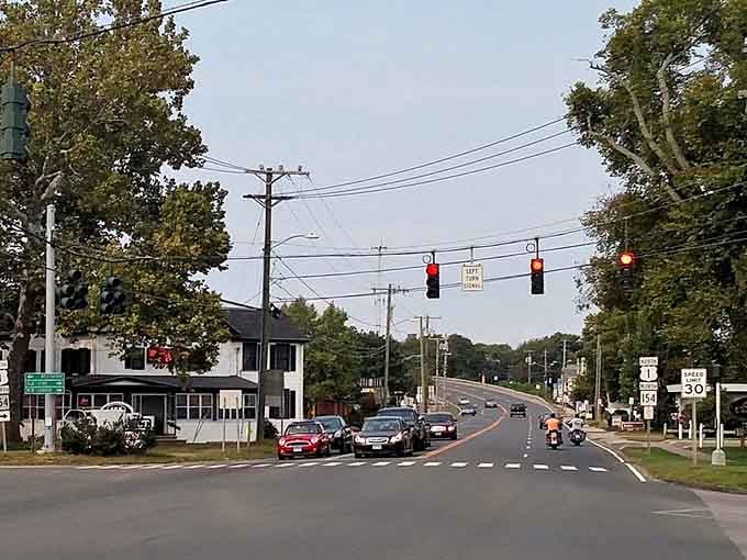 Enjoy a charming drive through historic Old Saybrook, where quaint buildings and leafy trees line the road on a peaceful day.