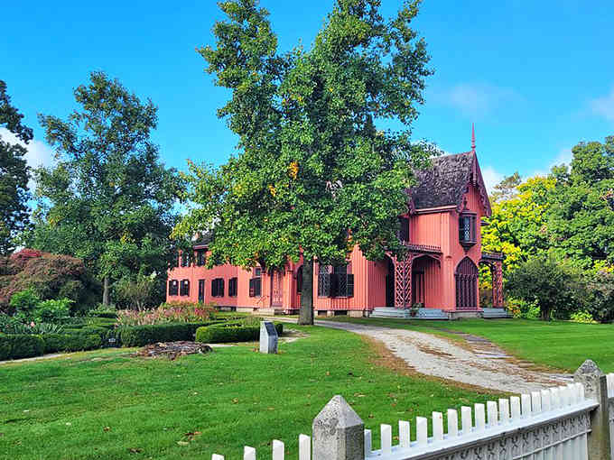 Ornate wooden trim adorns every corner of this salmon-colored mansion, where white picket fences frame a gravel driveway.