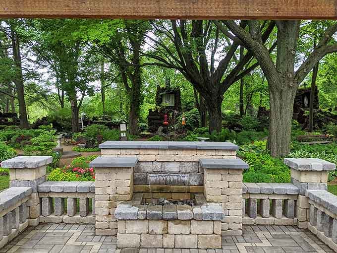 A serene fountain courtyard offers quiet reflection beneath towering trees and carefully stacked stone structures all around.