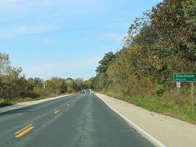 The open highway curves gently toward town, flanked by autumn trees that promise small-town hospitality just around the bend ahead.