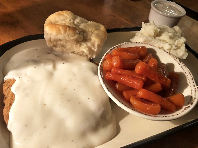 Country fried steak smothered in white gravy alongside fluffy biscuits and glazed carrots, pure comfort on one glorious plate.