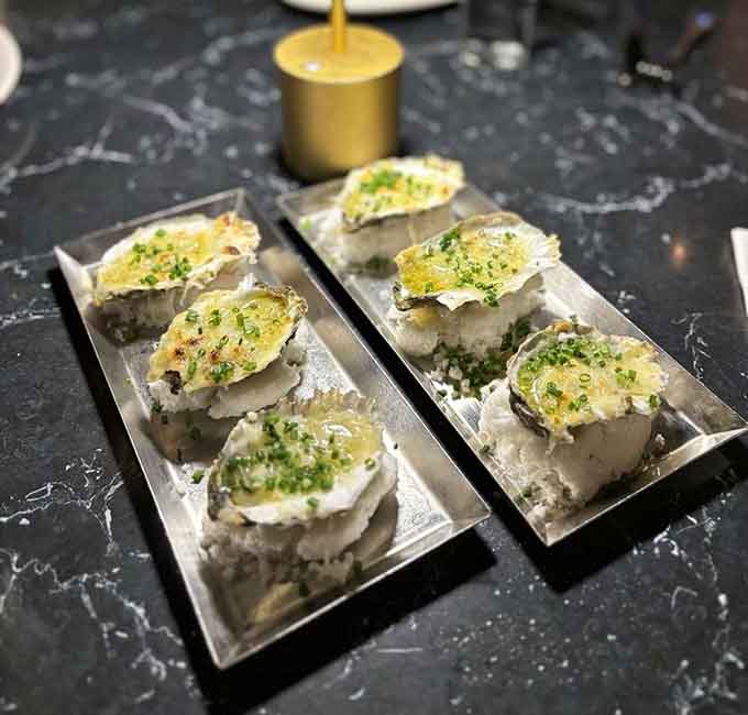 Oysters on the half shell gleaming under broiler-kissed toppings, briny perfection meets buttery indulgence beautifully.