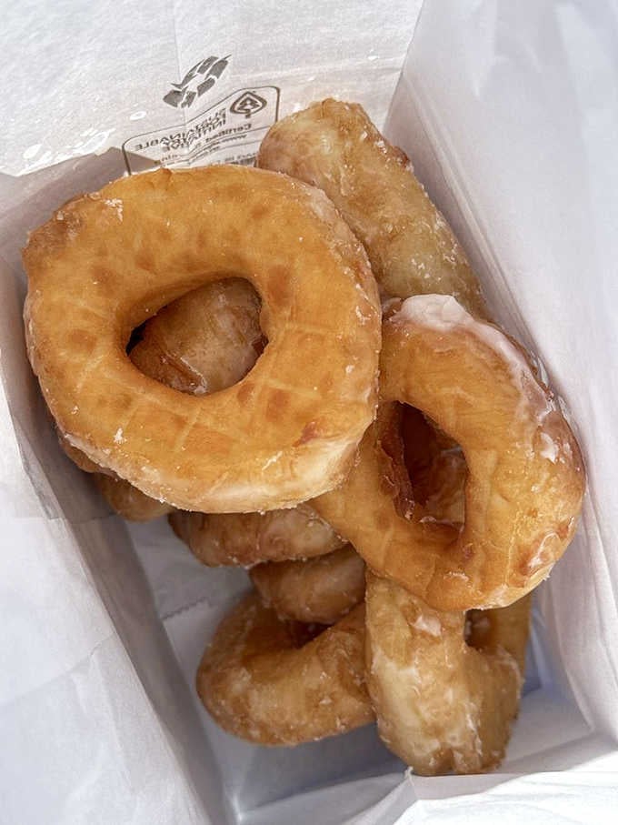 A box of glazed perfection, each donut slightly different but equally irresistible, ready for immediate consumption.