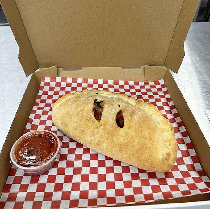 The calzone emerges golden and perfectly sealed, like a delicious envelope containing all your cheesy dreams inside.