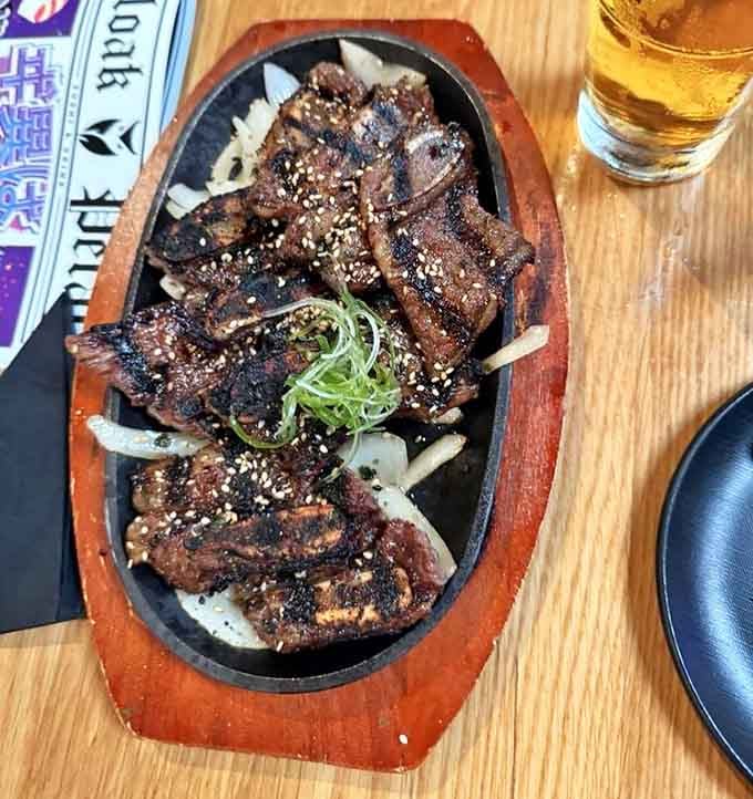 Kalbi short ribs sizzle on a wooden platter, their caramelized edges promising the kind of flavor that makes you close your eyes.