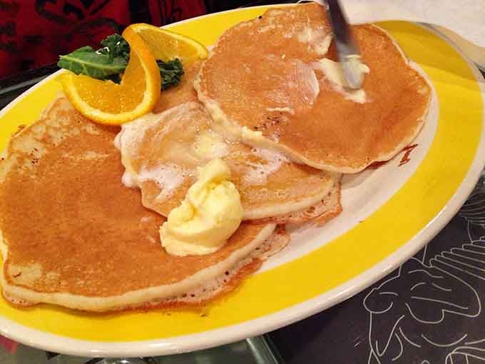 Pancakes stacked like they're trying to reach the curved ceiling, buttered and ready to make your morning absolutely magnificent.