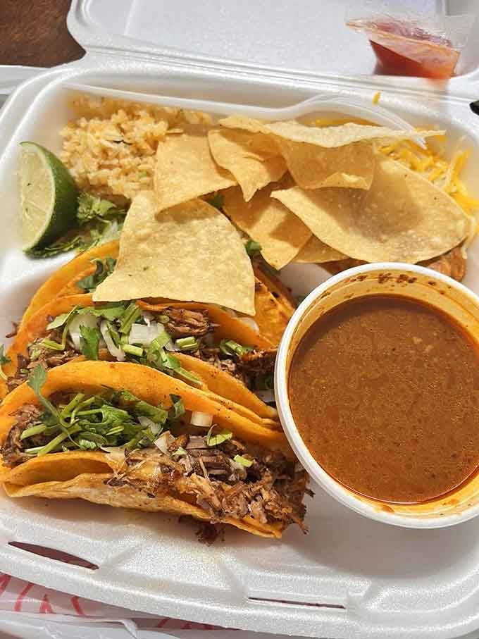 Quesabirria tacos with consomm&eacute; for dipping, tortilla chips, rice, and lime&mdash;this plate means serious business.