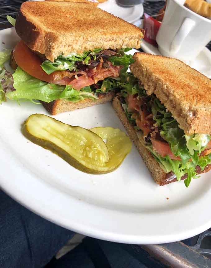 A BLT stacked so high it requires engineering skills to eat, served with a pickle spear.