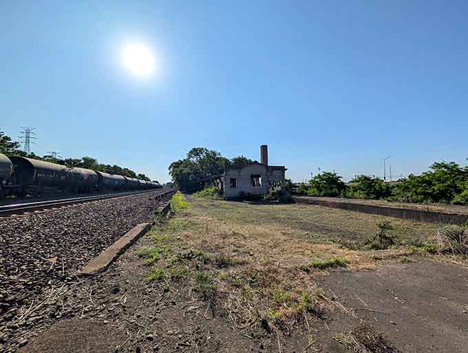 Active railroad tracks run past like time itself, indifferent to the silent witness beside them.