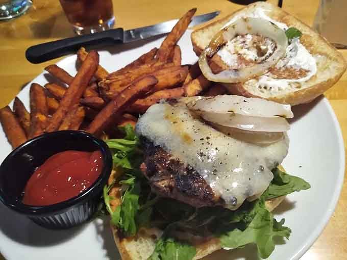 That burger sits under melted cheese like it's posing for its own magazine cover, sweet potato fries standing at attention.