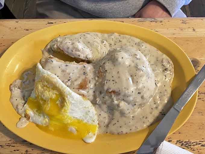 Biscuits drowning in sausage gravy with a sunny egg on top, proving that some Southern traditions are absolutely worth keeping.