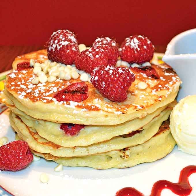 Fresh raspberries crowning fluffy pancakes like tiny jewels, proving breakfast can be both beautiful and delicious.