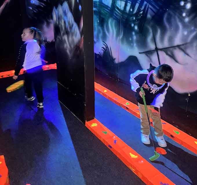 Young golfers concentrate on their putts while fluorescent murals create a backdrop that's pure Instagram gold for parents.