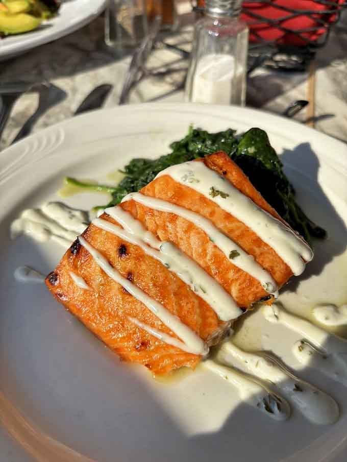 Perfectly seared salmon sliced to reveal its tender pink interior, draped with lemon butter sauce like edible silk over saut&eacute;ed spinach.