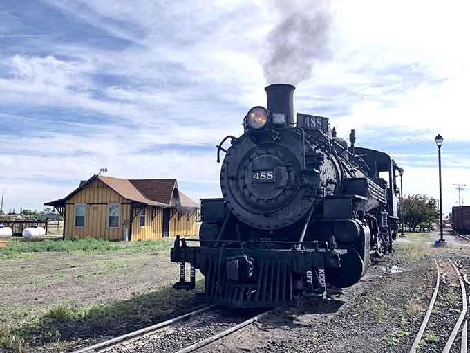 Steam pours from the smokestack as this magnificent black locomotive sits beside a weathered wooden depot building at dawn.