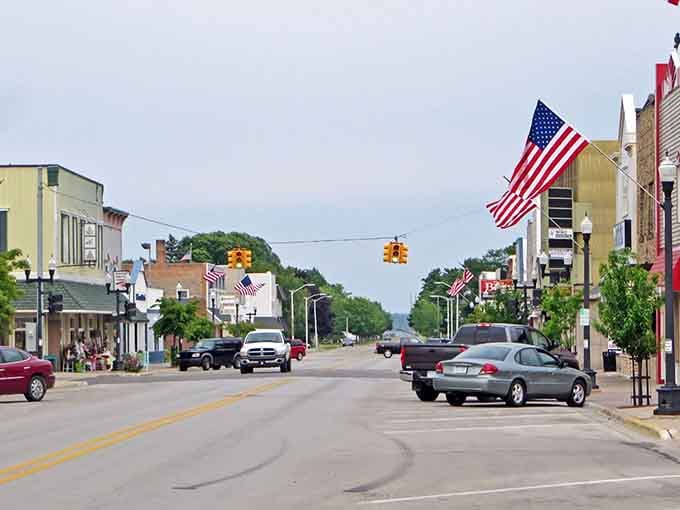 Stars and stripes wave proudly above main street where green hills roll in the distance beyond welcoming storefronts.