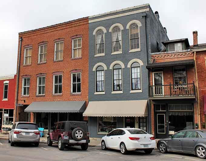 The blue-gray building stands shoulder-to-shoulder with its brick neighbors, their arched windows watching over generations of Main Street shoppers.