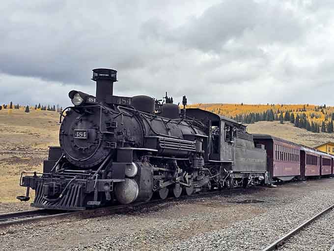 Golden aspens glow against stormy skies while the steam engine rests, creating a moody autumn scene worthy of Ansel Adams.