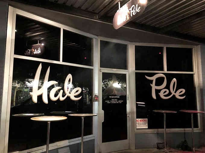 Evening transforms the storefront into a glowing beacon where tiki dreams come alive behind those inviting glass doors.