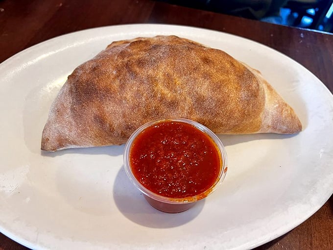 The calzone arrives golden-brown and stuffed, a portable pocket of Italian goodness begging to be devoured immediately.