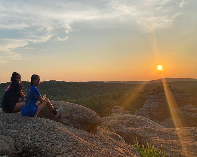 Two friends perched on ancient rocks watch the sun melt into the horizon, creating memories that'll outlast their phone batteries.