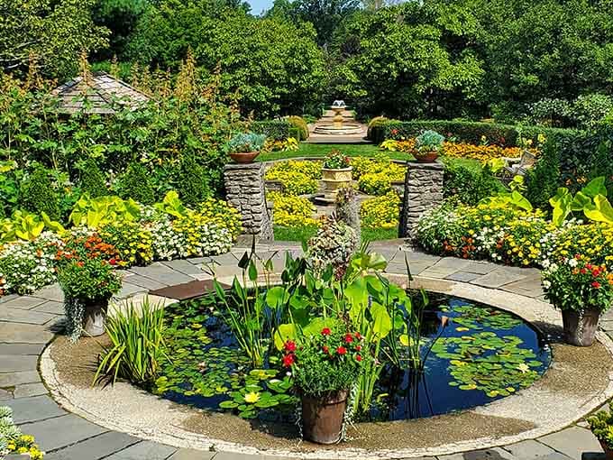 A serene circular pond filled with floating lilies sits nestled among blooming flower beds and lush greenery in this paradise.