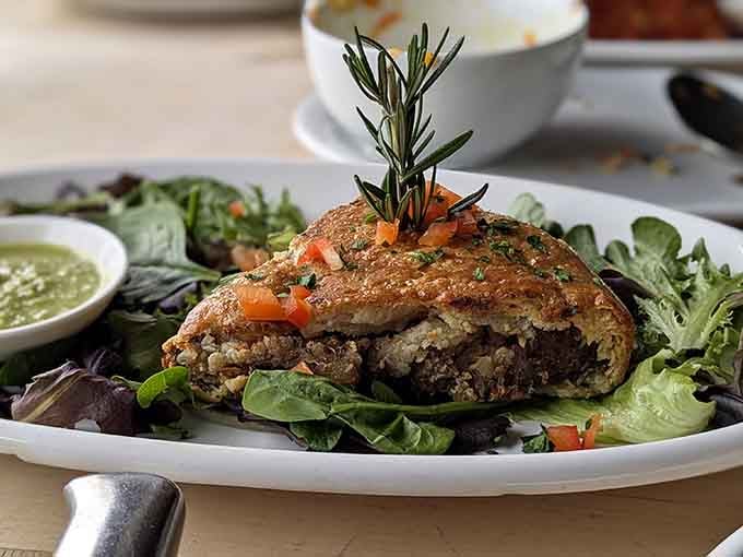 A beef pot pie nestled on greens with rosemary garnish, looking like it belongs in a food magazine.