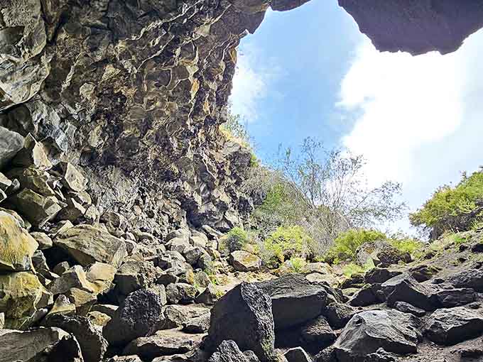 Looking up from inside reveals blue sky framed by jagged volcanic rock, a portal to another world.
